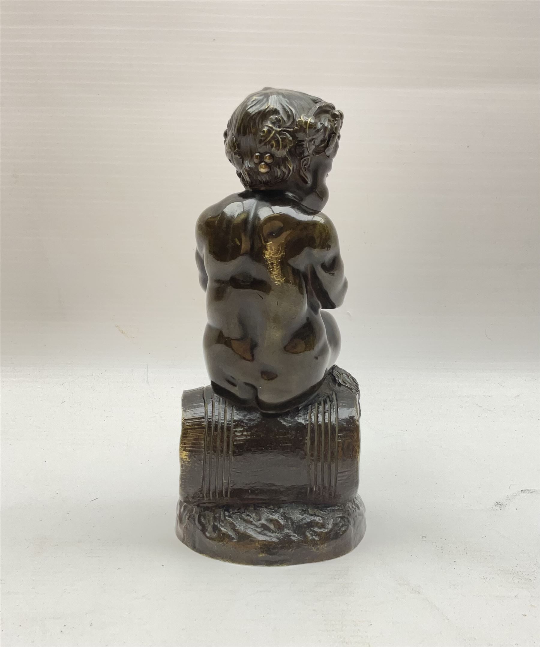 Bronzed metal model of a putti seated upon a barrel with goblet in ...