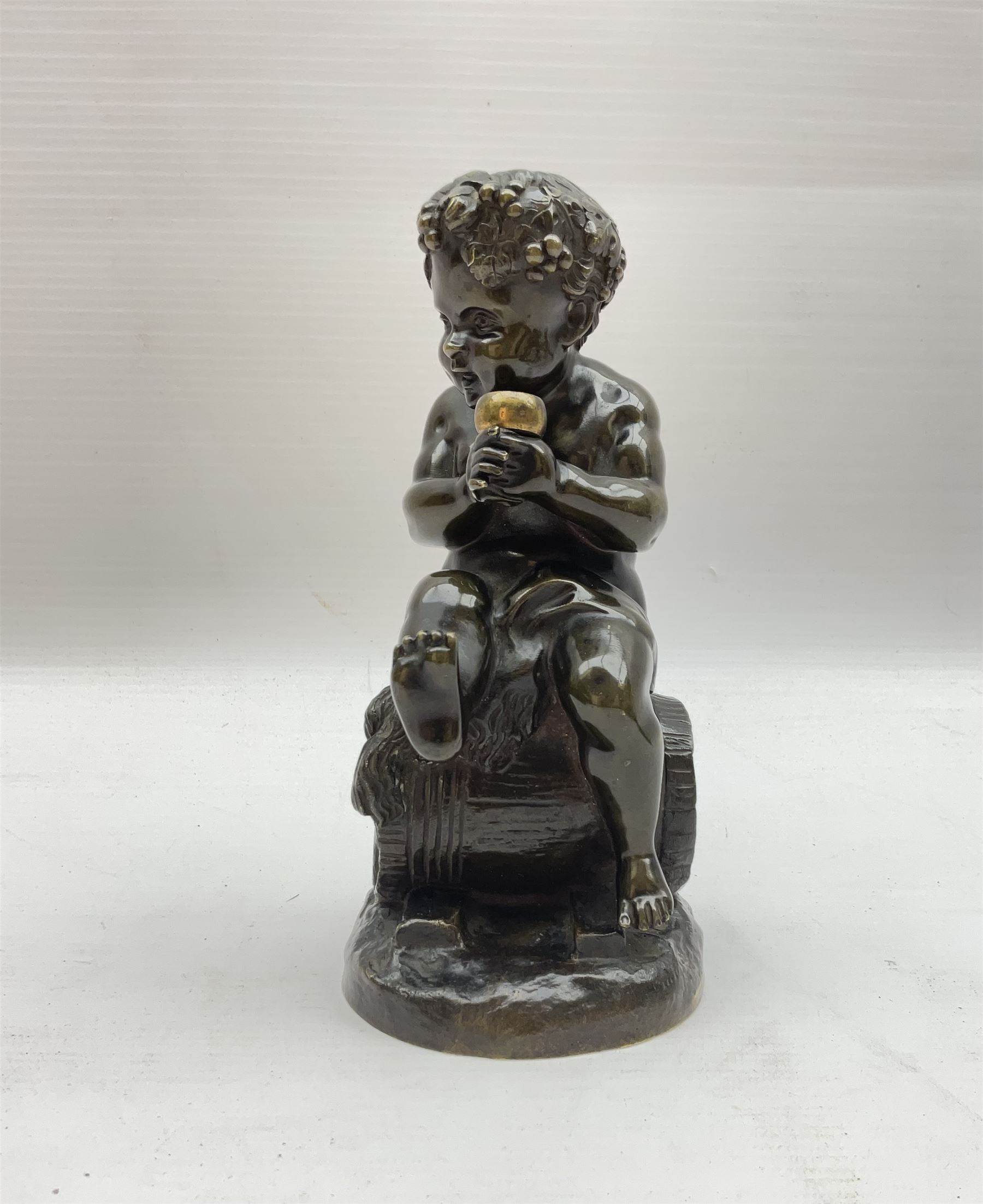 Bronzed metal model of a putti seated upon a barrel with goblet in ...